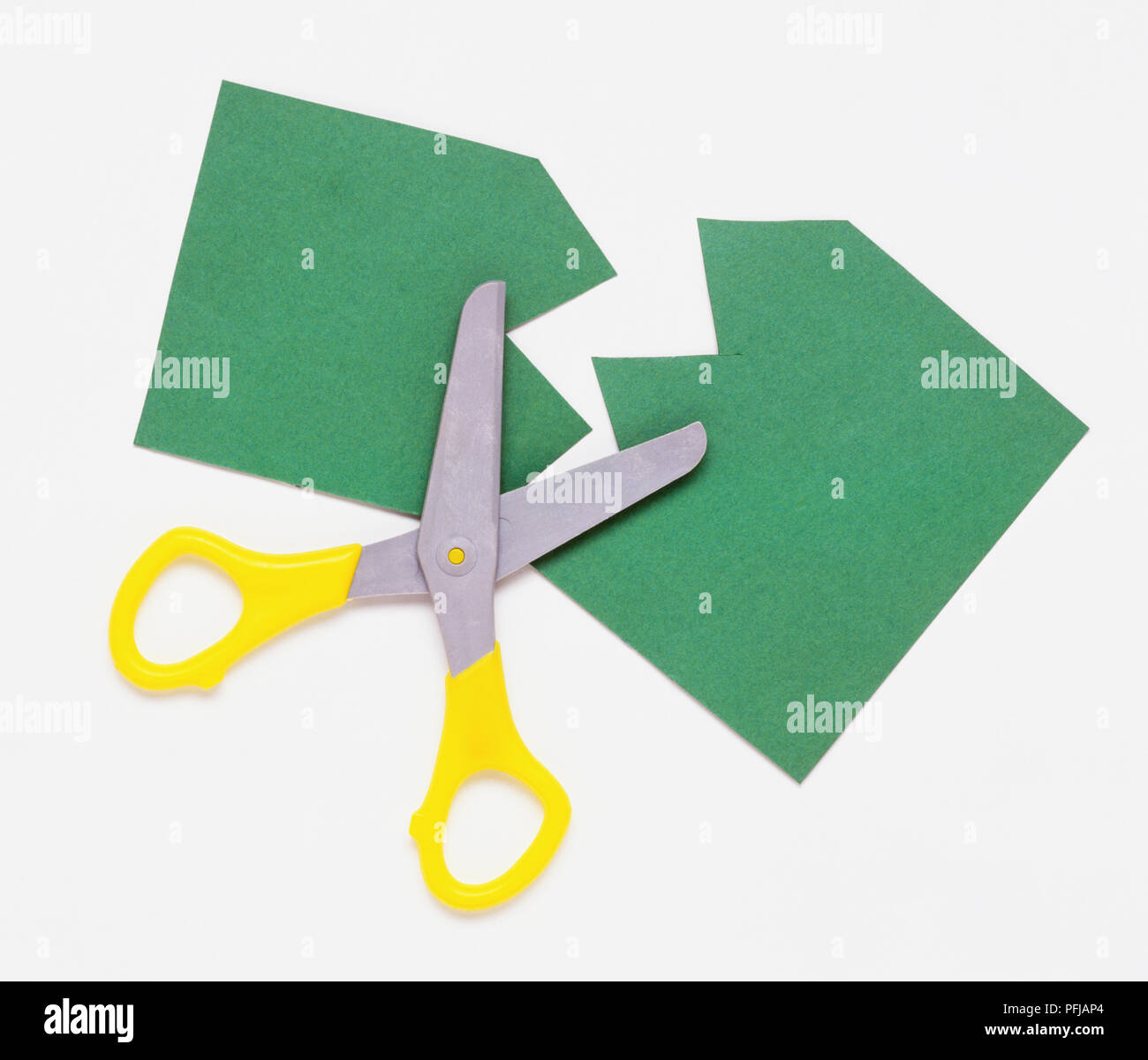 Green paper cut up in ziz-zag pattern, and pair of yellow scissors ...