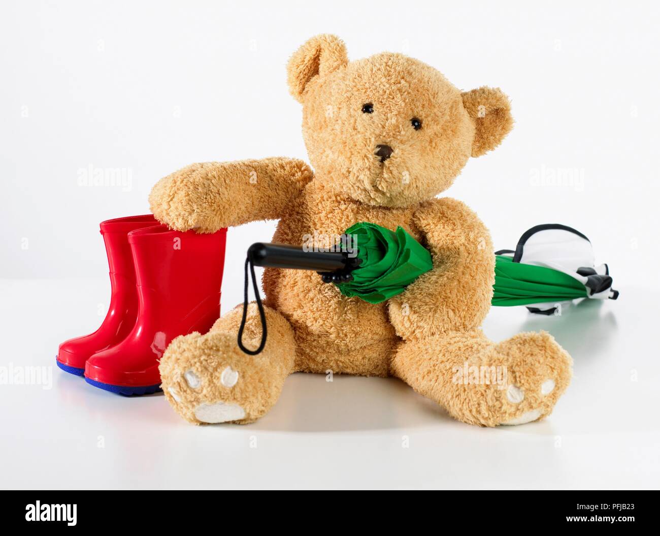 Teddy bear with umbrella under the am, next to a pair of wellington ...