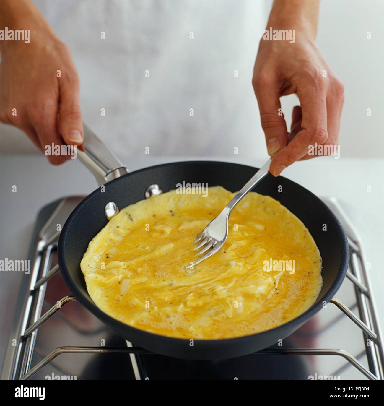Omelette cooking in a frying pan, using a fork to stir egg Stock Photo ...