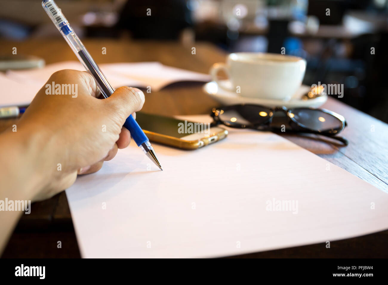 Man left handed writing in note with pen on paper with cell phone and ...