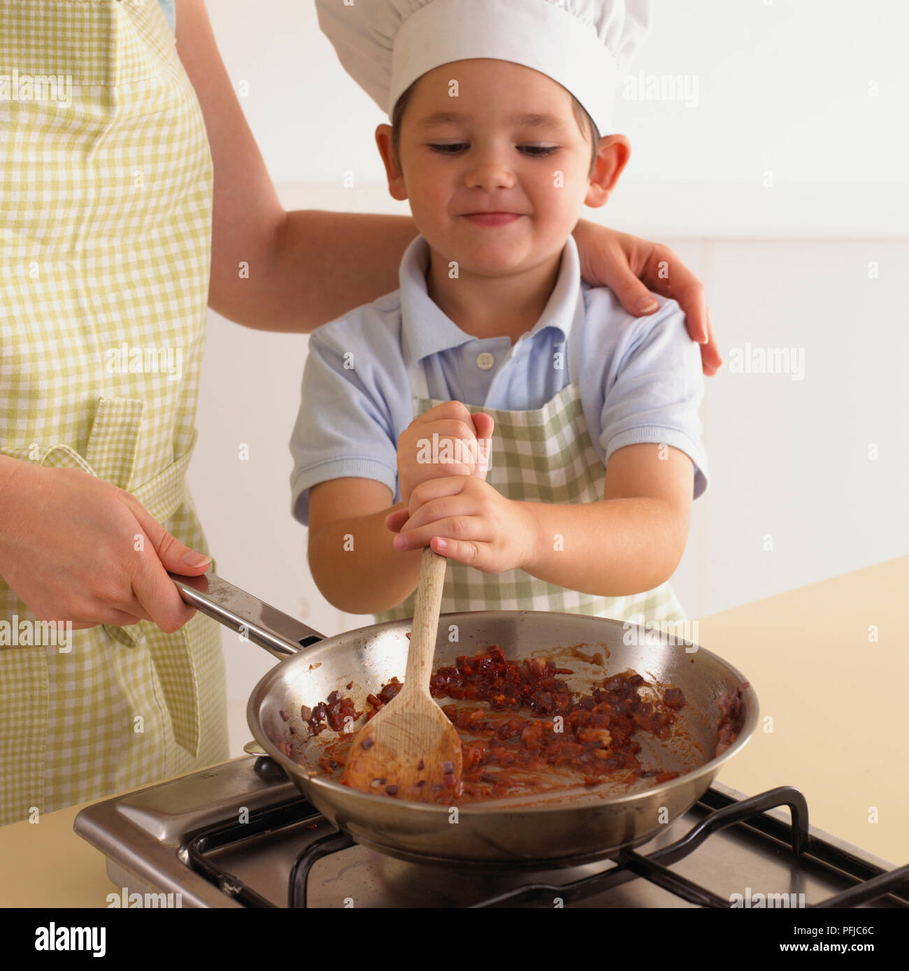 Boy stirring tomato sauce in saucepan, assisted by his mother Stock ...