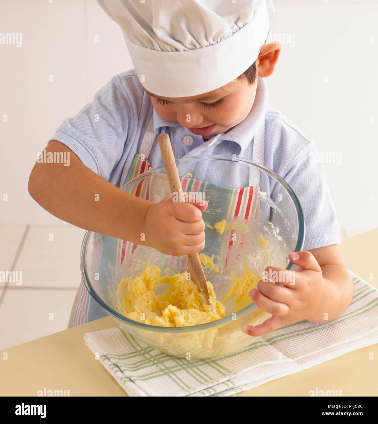Boy in chef's hat beating together butter, eggs and sugar in mixing ...