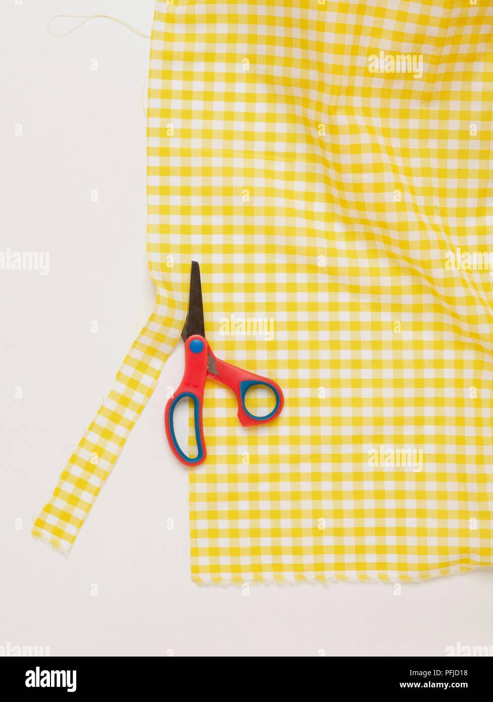 Scissors cutting strip off yellow checked fabric to make a straight ...