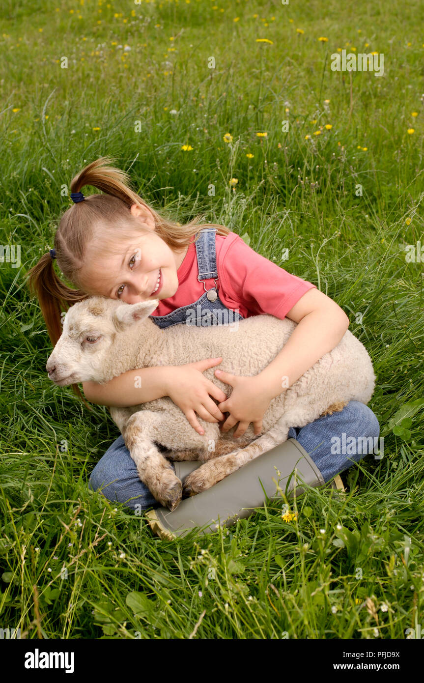 Young girl sitting on grass hugging lamb Stock Photo - Alamy