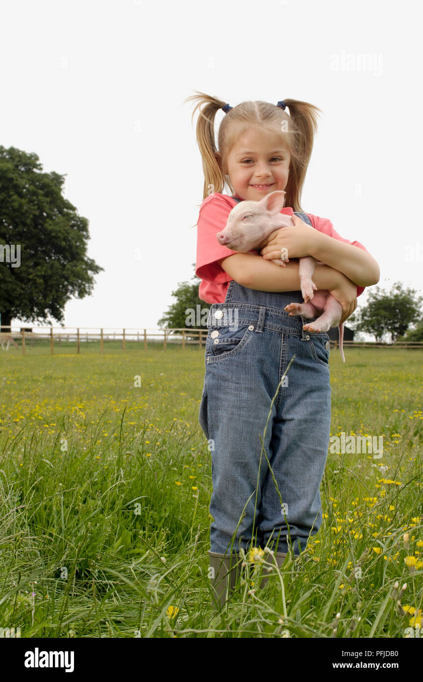 Young girl standing in field holding piglet Stock Photo - Alamy