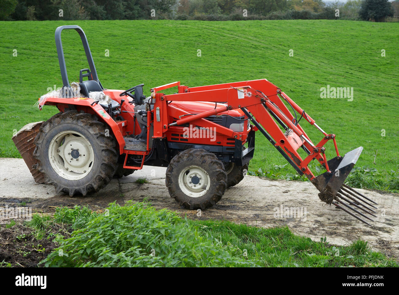 Red tractor on a path amidst fields Stock Photo - Alamy