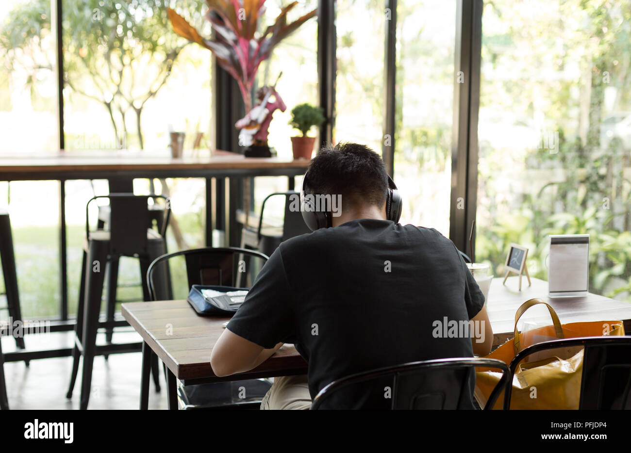 Asian student studying in the cafe with headphones listening to music ...