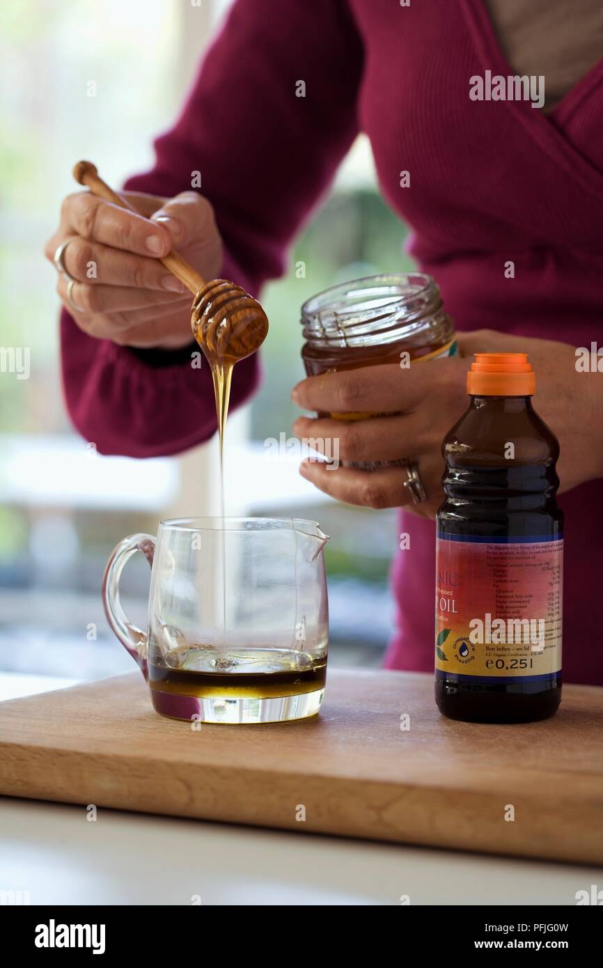 Woman's hand dripping honey into camomile tea and hemp oil mixture in ...