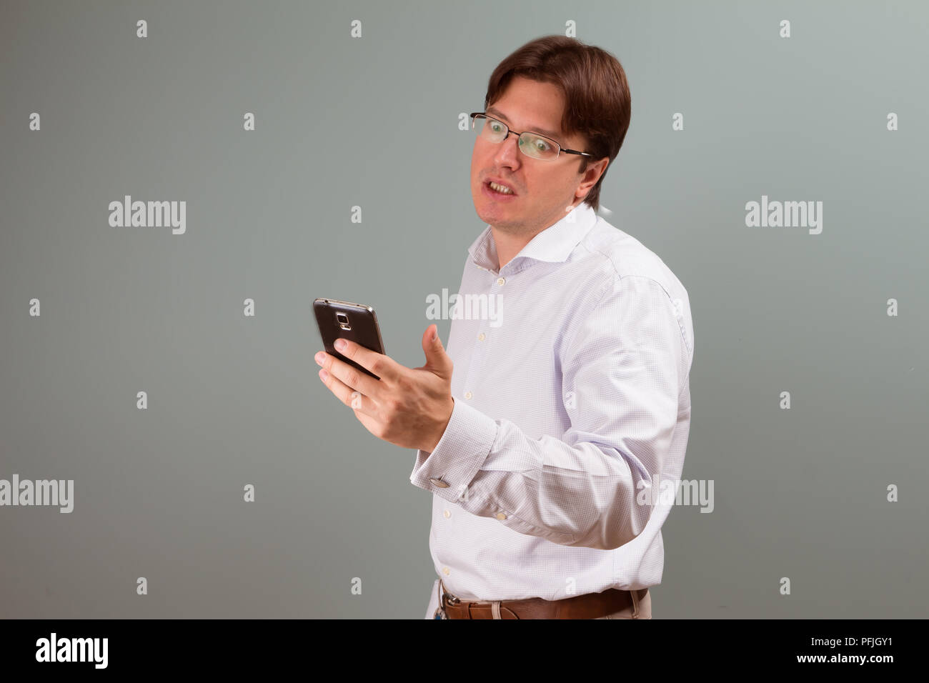 an angry young man looks at his phones's screen; studio portrait with ...