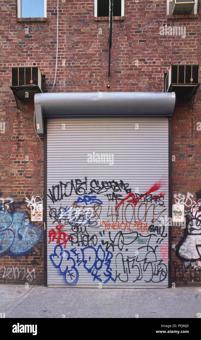USA, New York, brick building with metal gate covered in graffiti ...