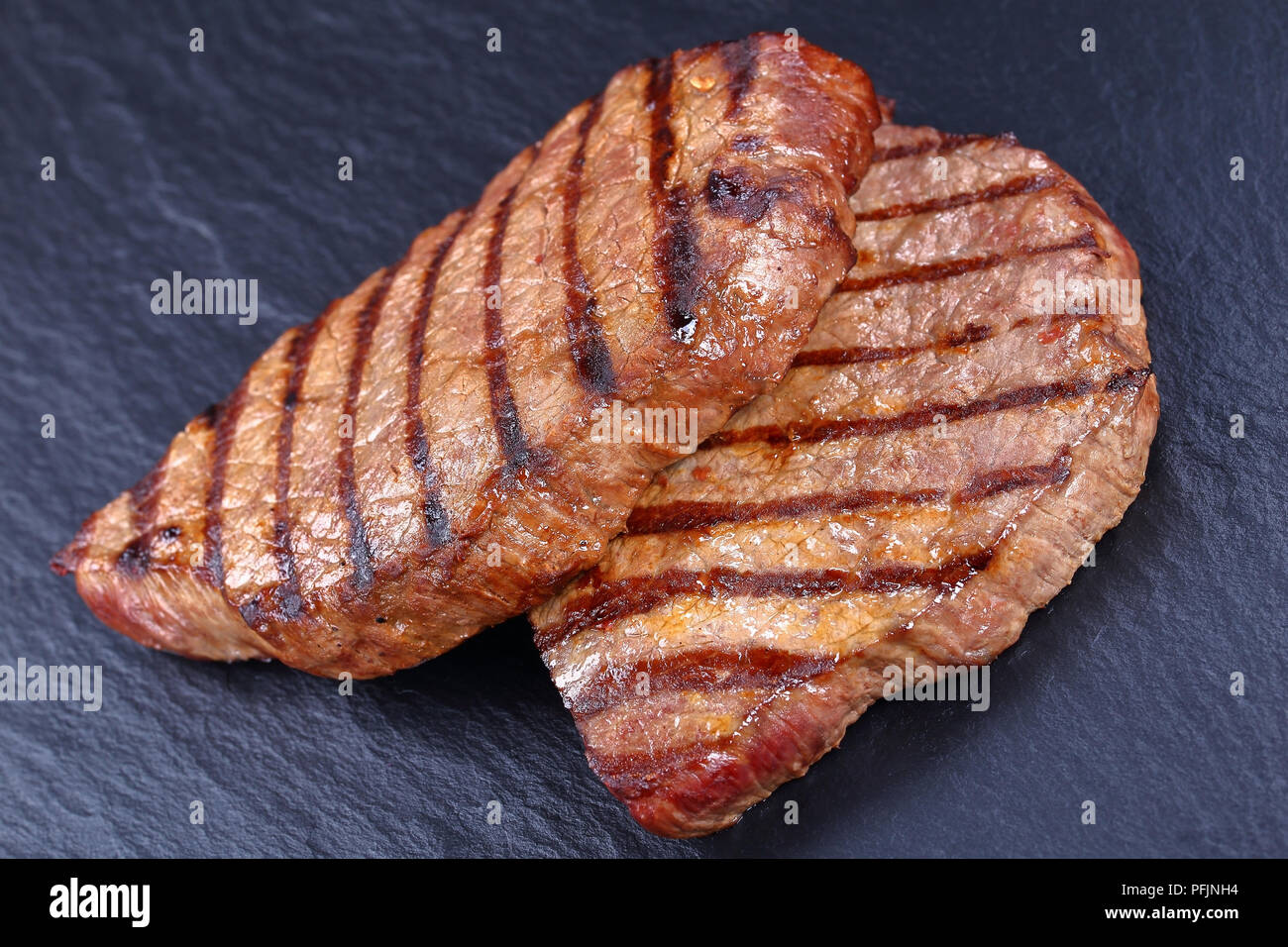 close-up of hot delicious barbecued beef steaks with stripes on black ...