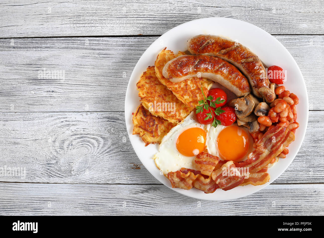 full hot english breakfast - bean, hash brown, fried eggs sunny side up, bacon slices, sausages ...