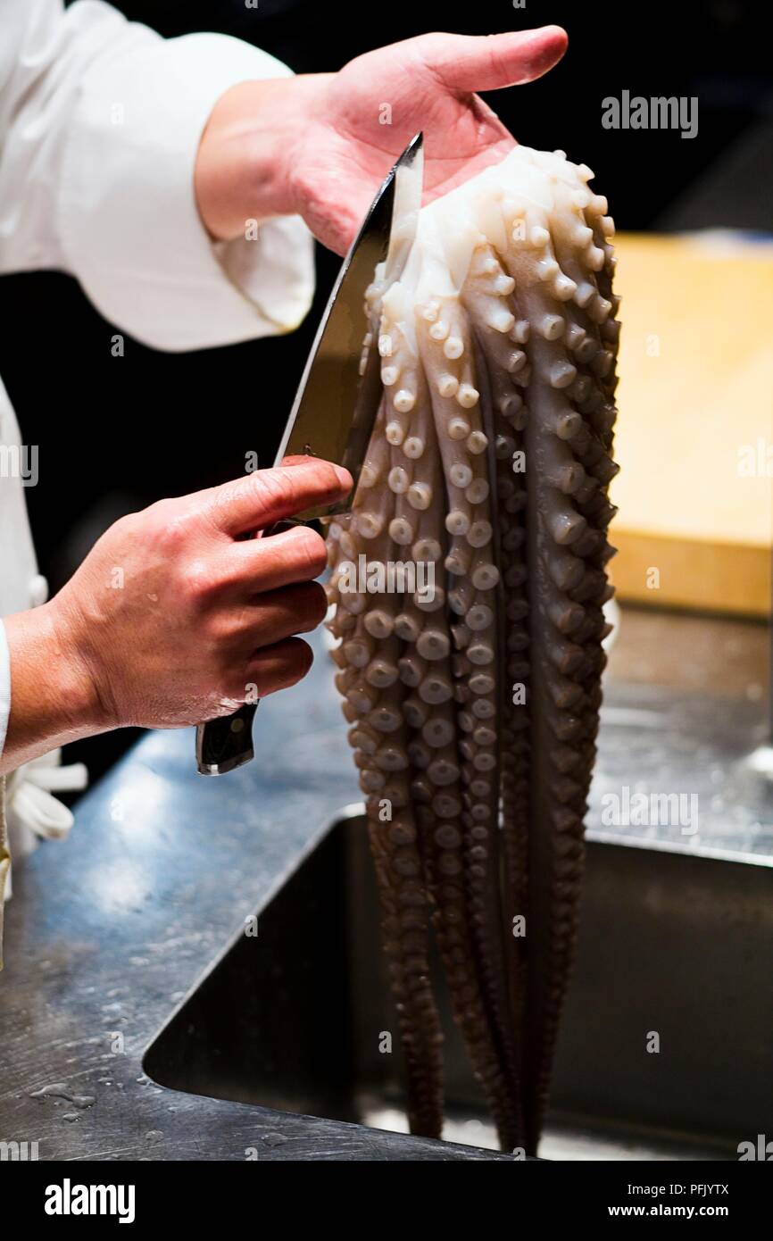 Chef scoring top of tentacles of octopus, using large kitchen knife ...