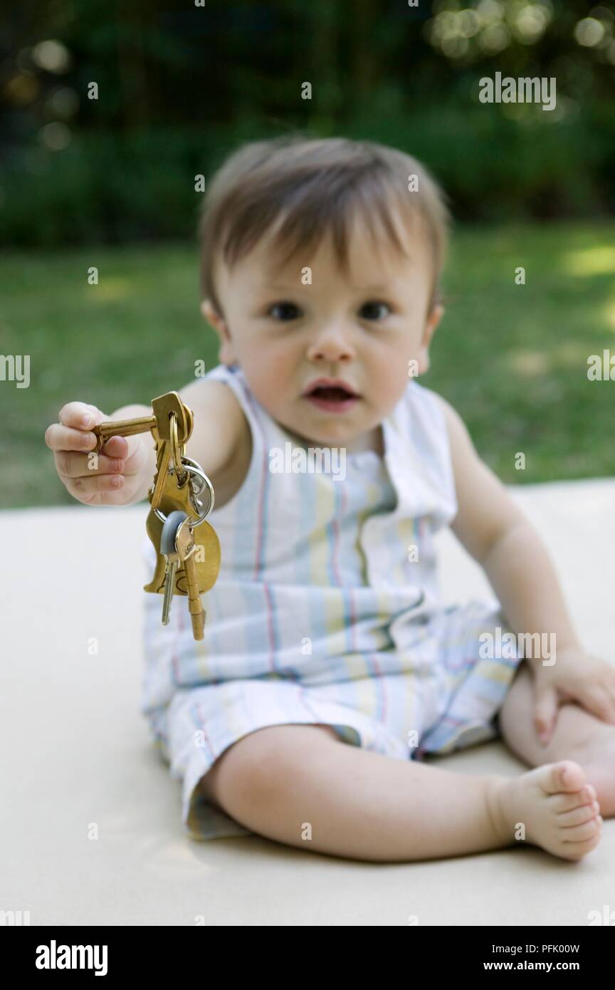Baby boy sitting on blanket in garden holding set of keys, looking at ...