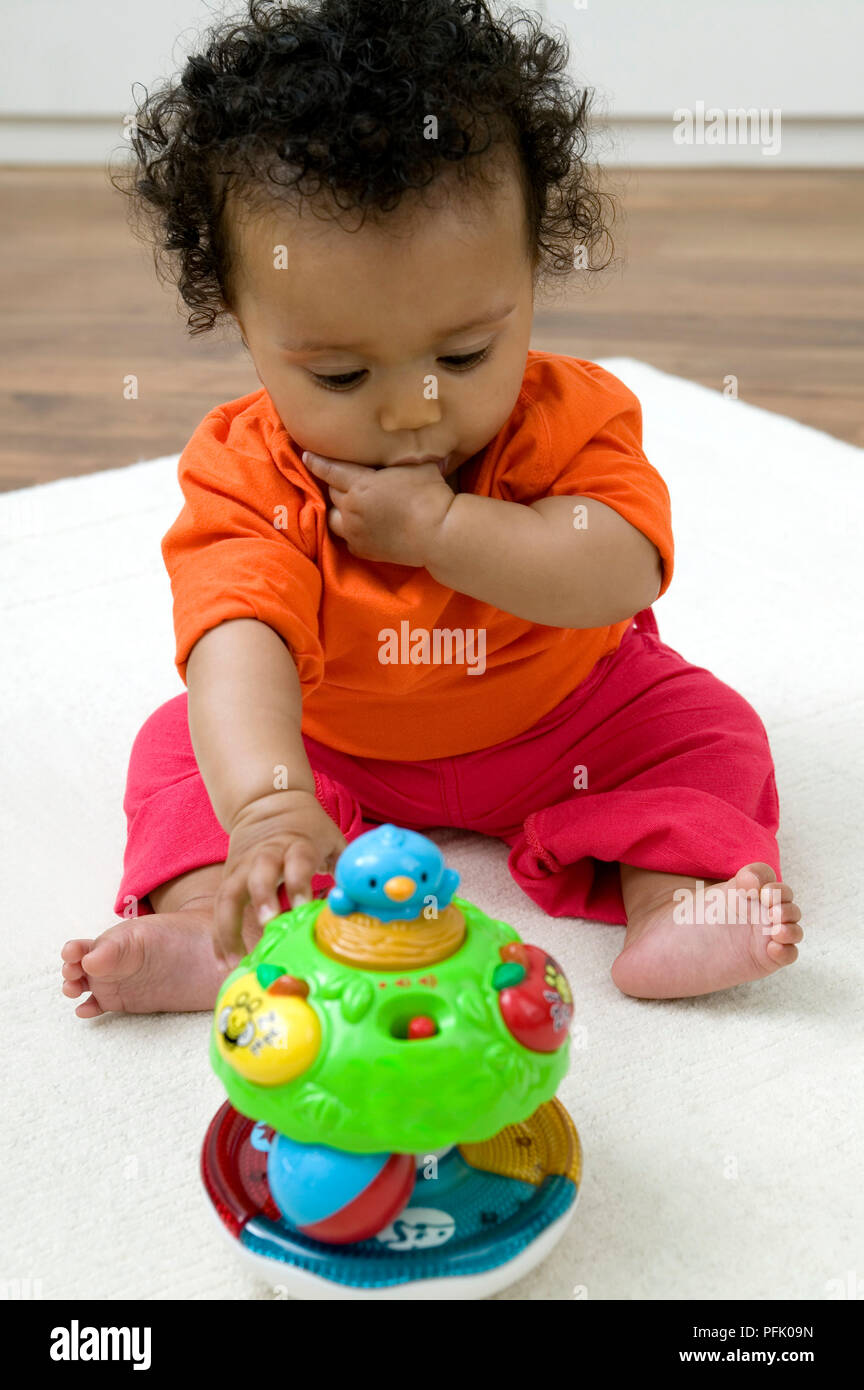 Baby girl sitting on rug playing with plastic toy Stock Photo - Alamy