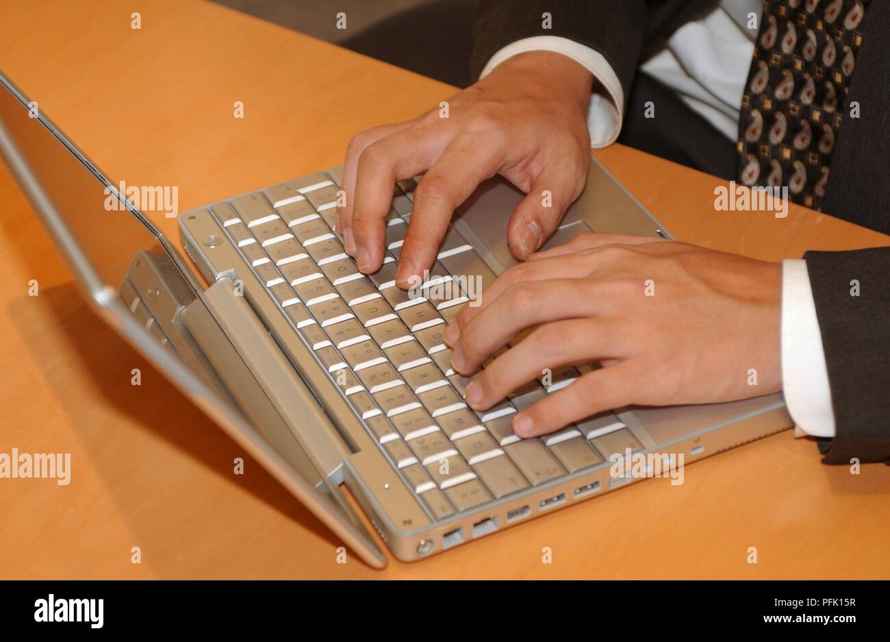 Businessman sitting at desk and typing on small laptop Stock Photo - Alamy