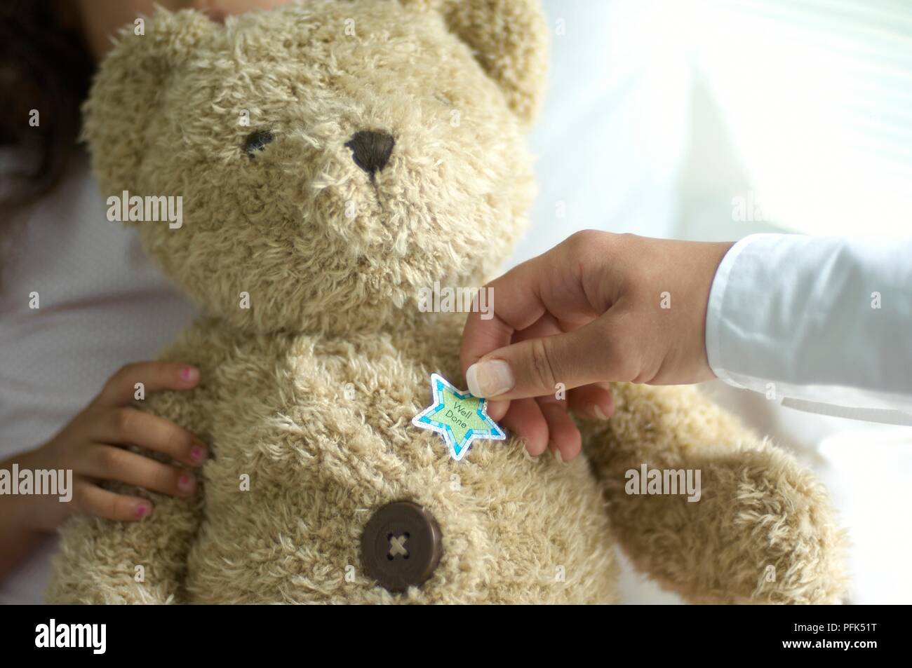 Girl's hand holding teddy bear, woman's hand sticking on 'well done ...
