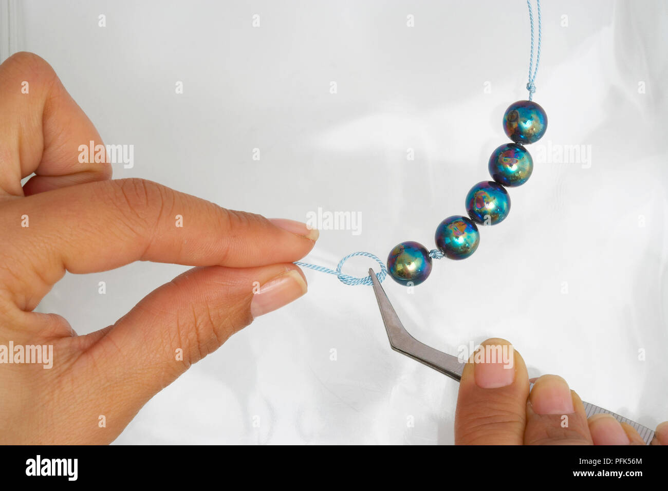 Threading fifth bead onto stringing wire and knotting blue thread with ...