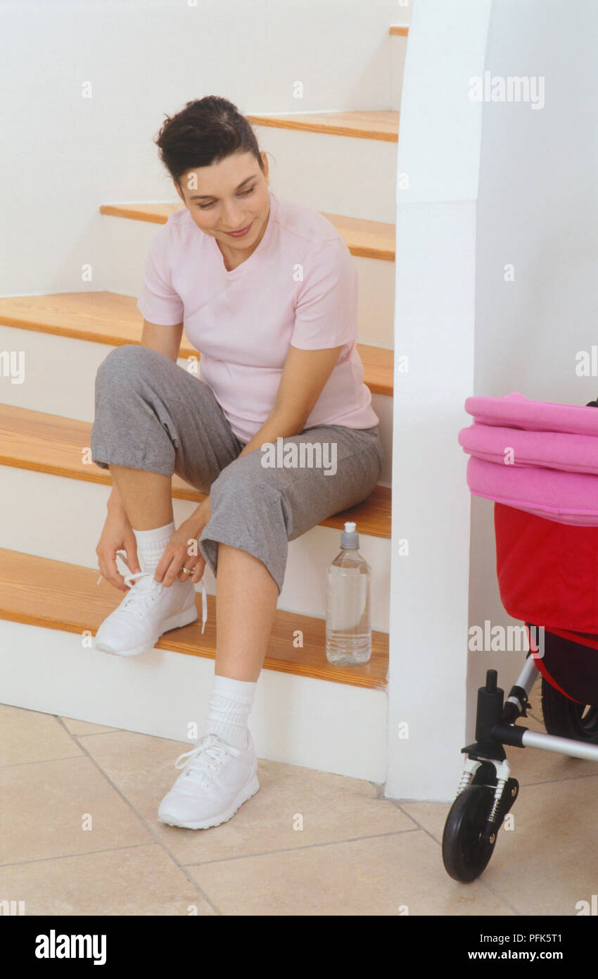 Woman sitting on step tying shoelaces, looking at pram Stock Photo - Alamy