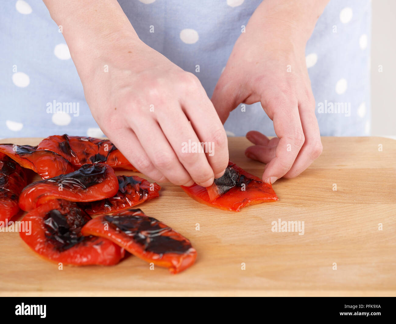 Young woman's hands peeling off blackened skin off red bell peppers ...