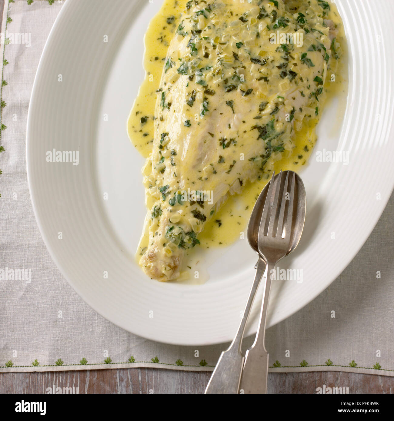 Grilled flat fish in butter and herb sauce, on serving plate with spoon ...