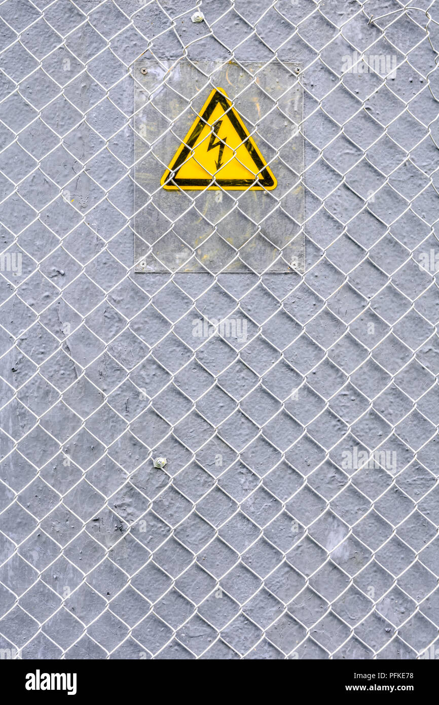 Danger of electrocution yellow sign on gray background with metal wire ...