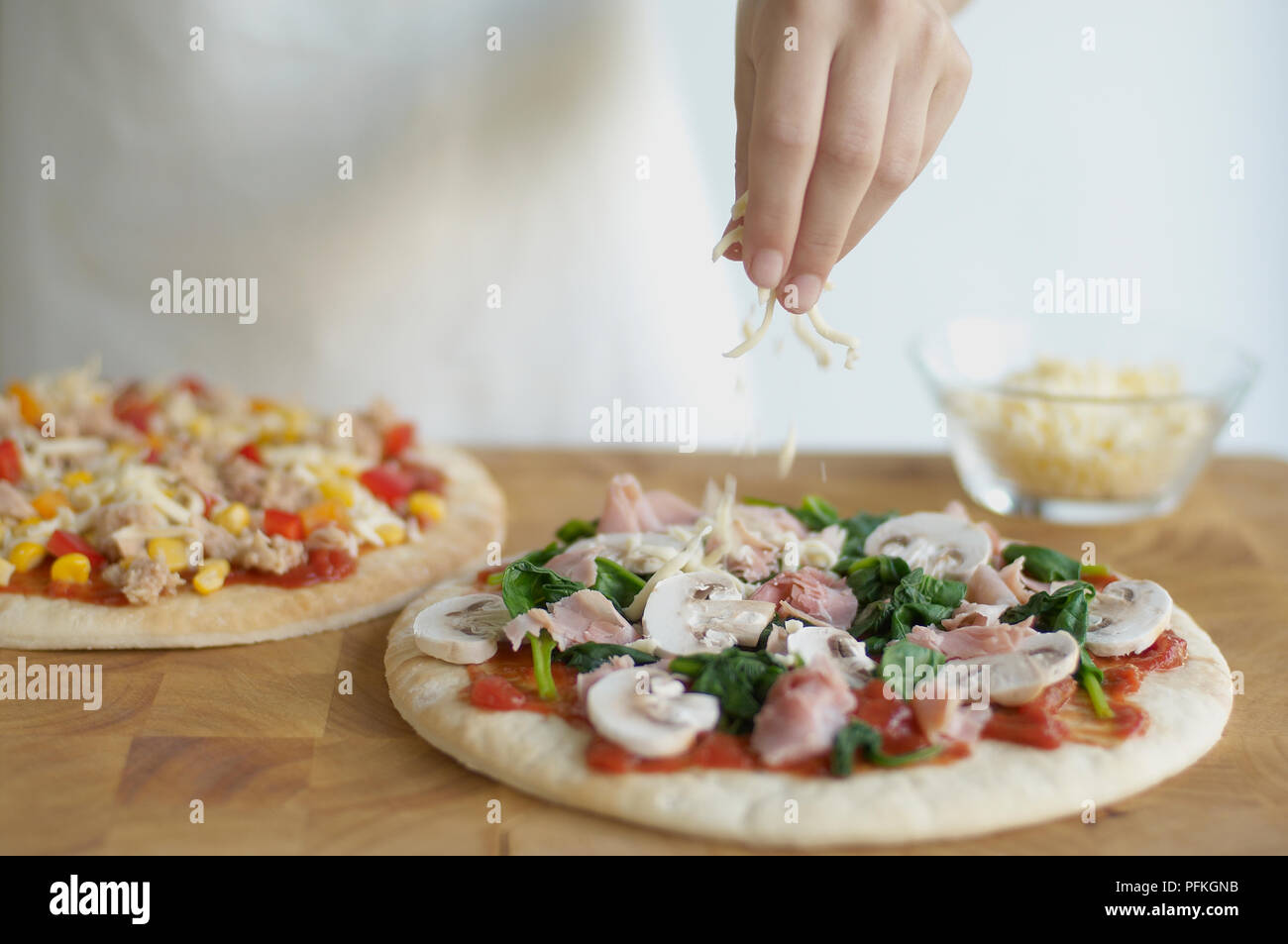 Adding grated cheese to ham and mushroom pizza, with tuna and sweetcorn ...