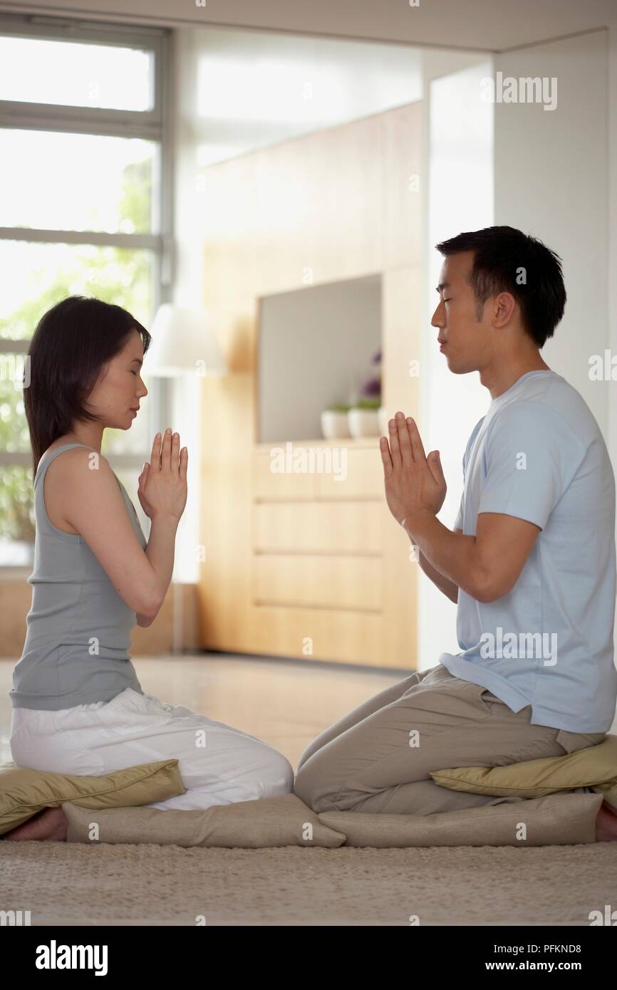 Woman and man kneeling opposite each other on floor, hands folded, side ...