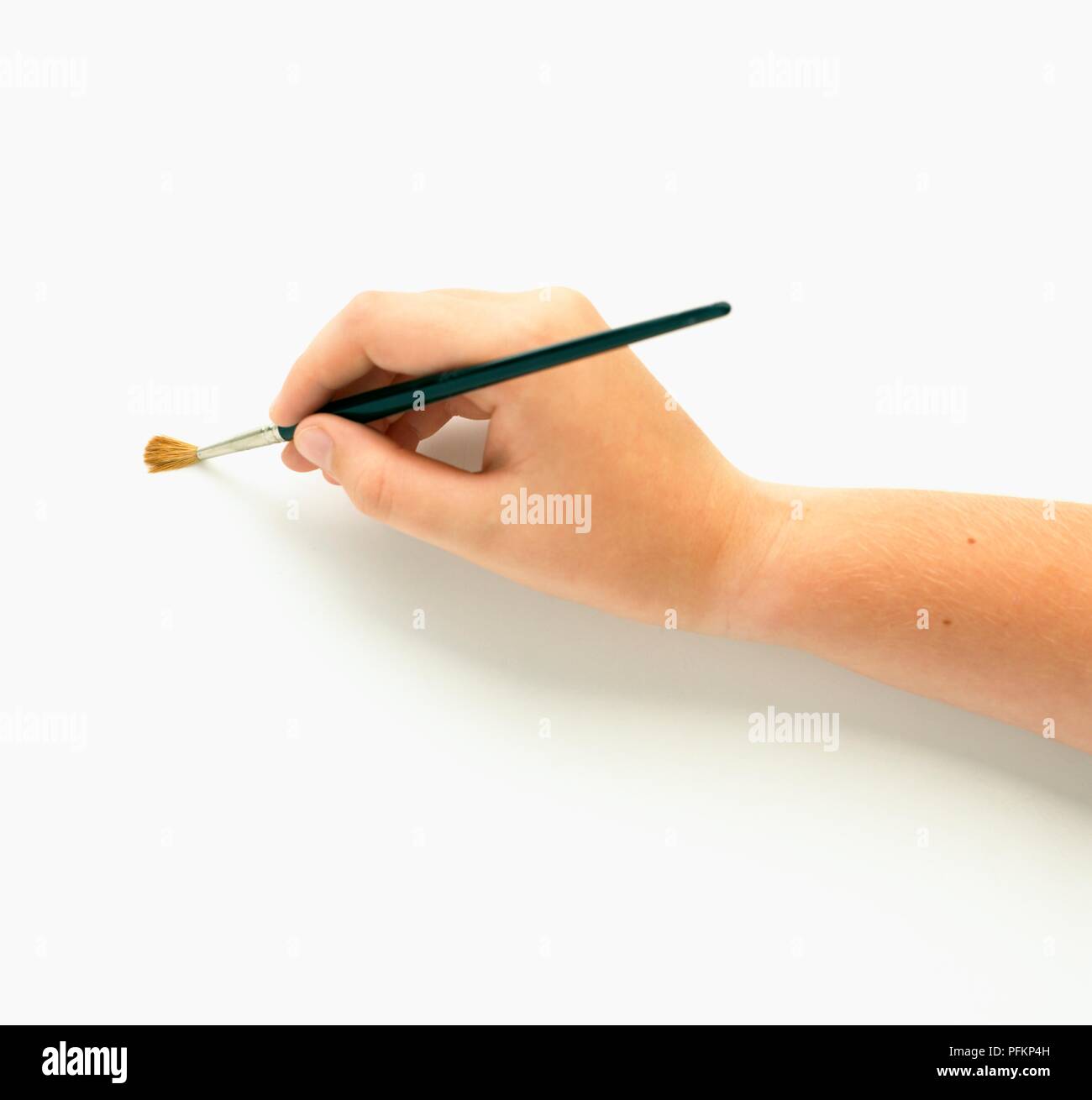 Boy's hand holding paint brush against white surface Stock Photo - Alamy