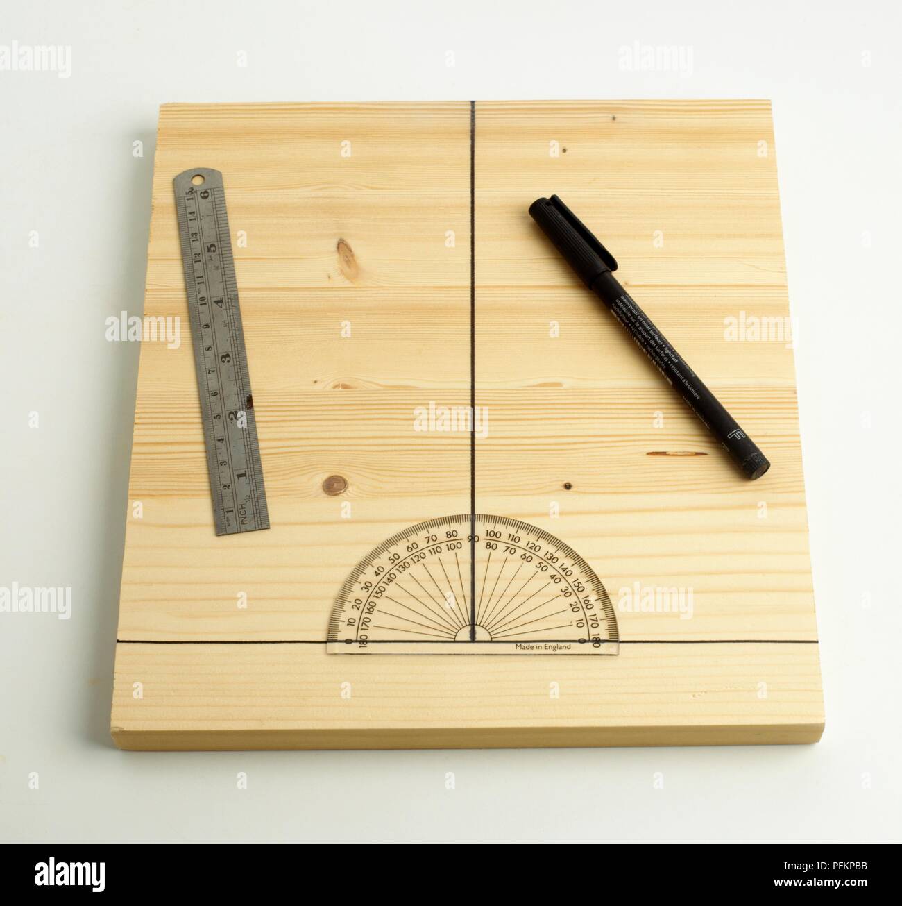 Protractor, ruler and pen on block of wood with black lines drawn on ...