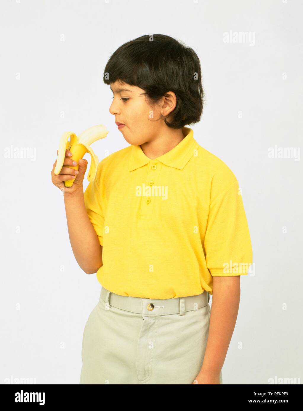 Boy in yellow polo shirt eating banana, looking away Stock Photo - Alamy