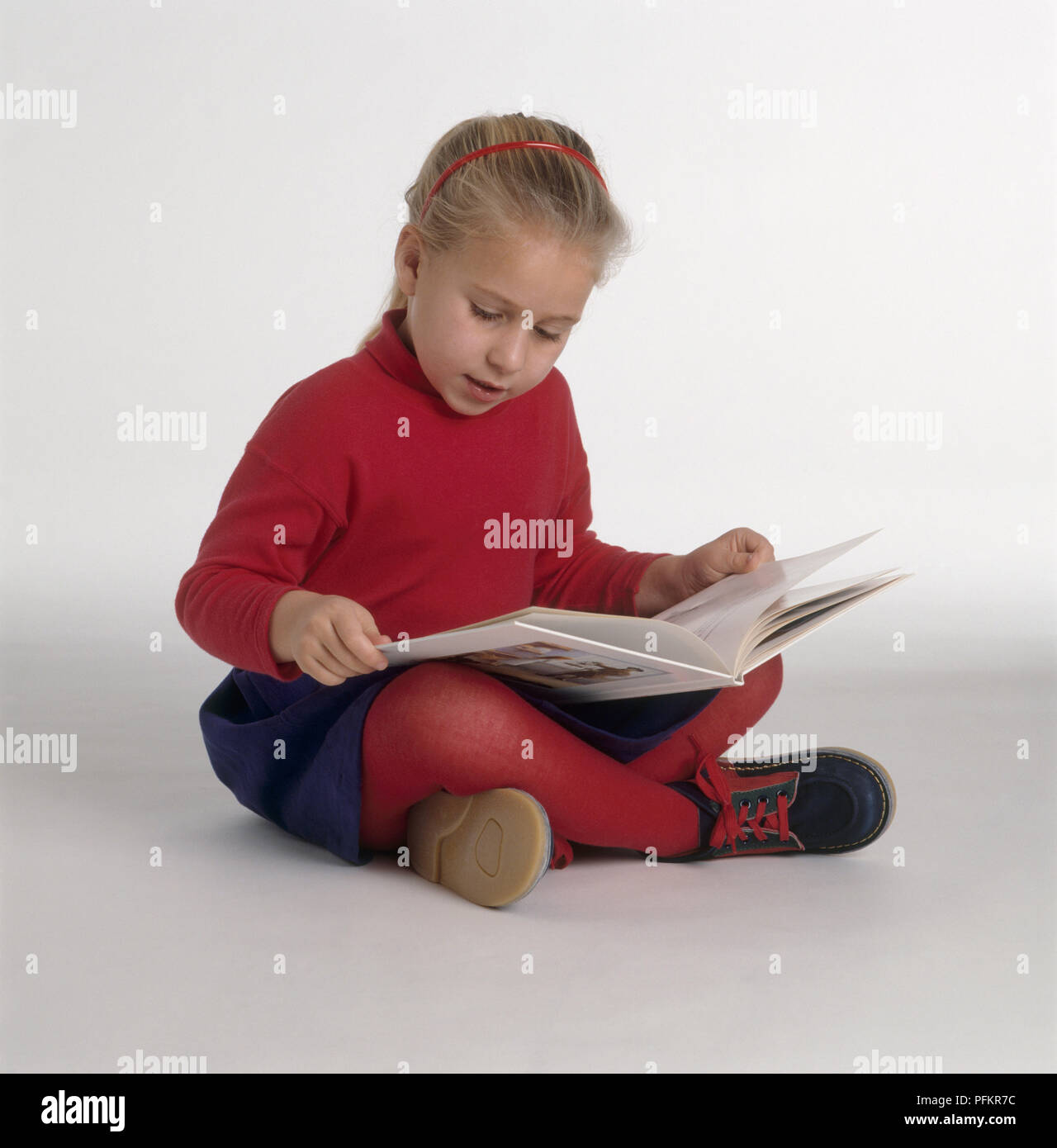 Girl reading book while sitting on the floor with her legs crossed ...