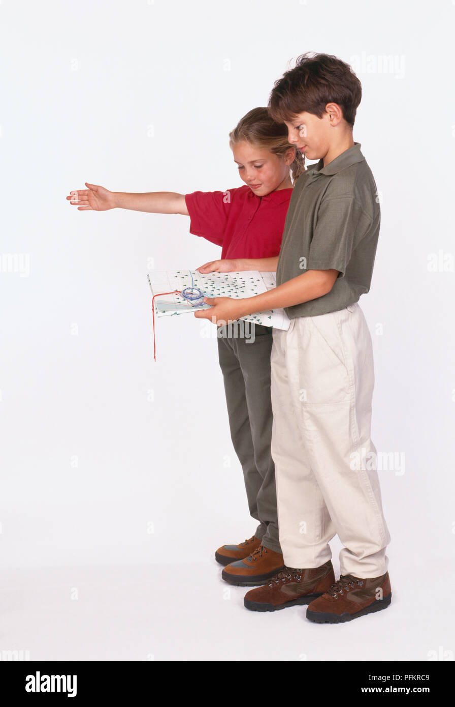 Boy and girl standing holding map, girl pointing with her arm, side ...