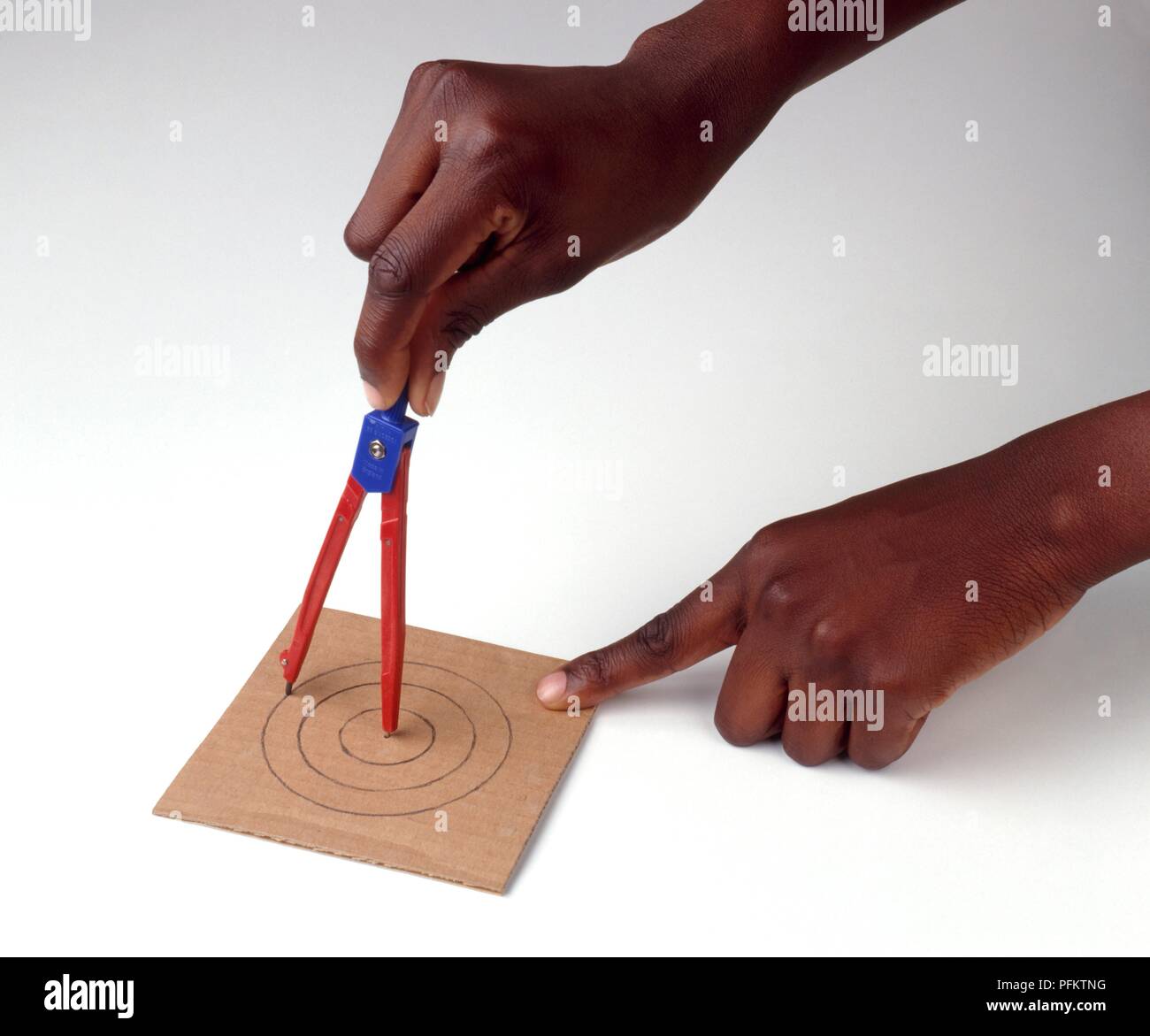 Boy's hands drawing circles on piece of cardboard with a compass, close ...