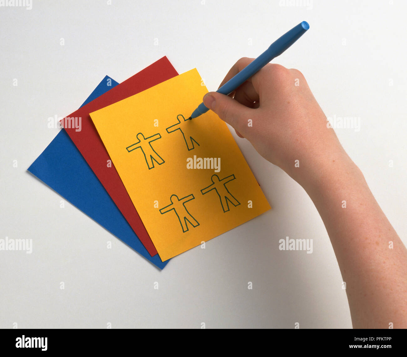 Child using blue felt tip pen to draw stick figures on yellow paper ...
