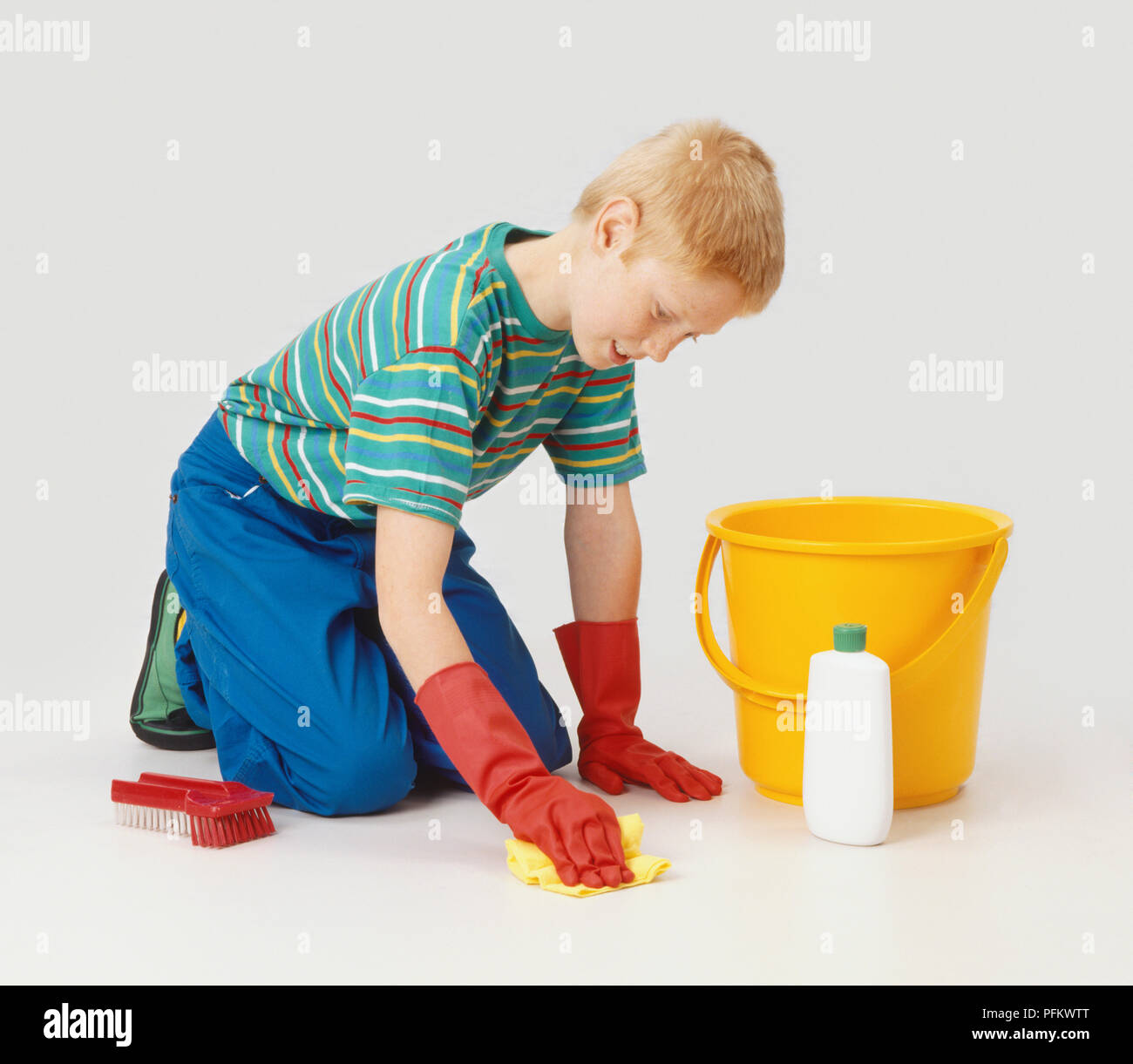 Blonde boy wearing red rubber gloves kneeling by yellow bucket and ...