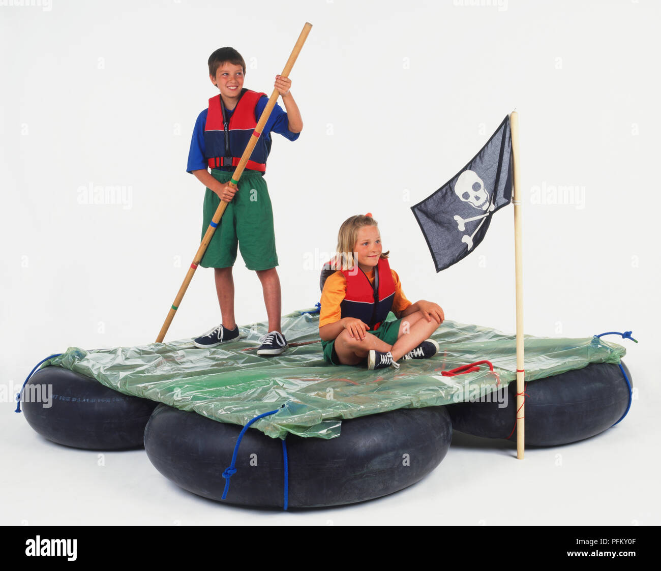 Boy standing and girl sitting on raft, pirate flag attached to front ...