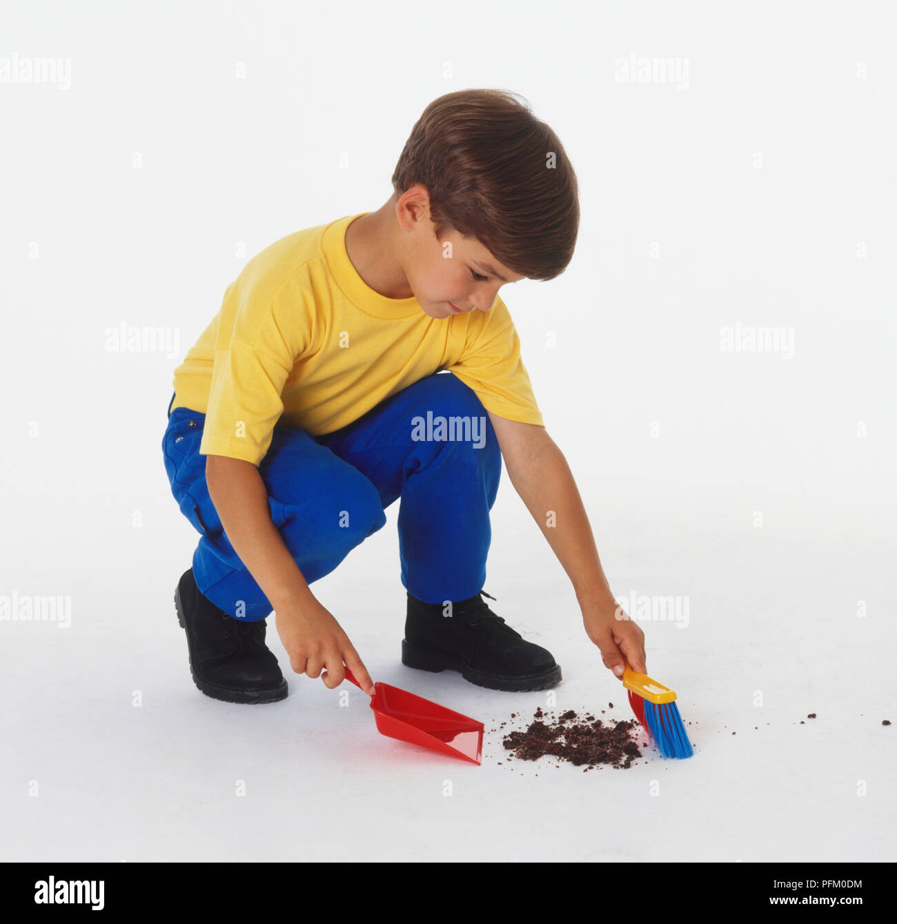 Boy crouching to use dust pan and brush to sweep up dirt Stock Photo ...
