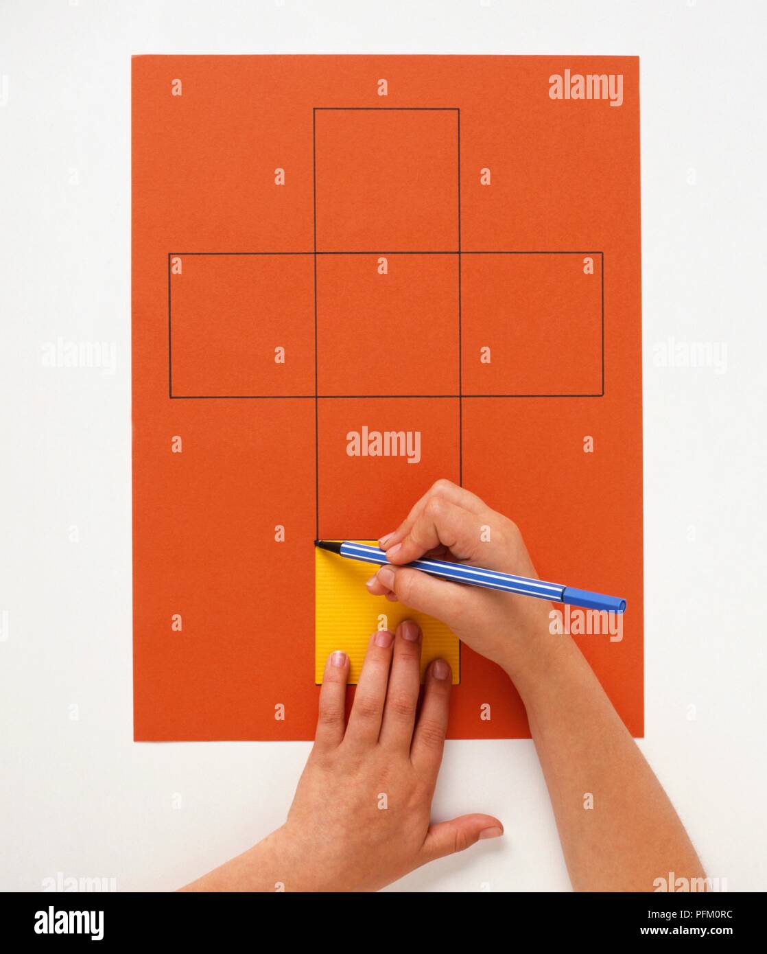 Boy's hand drawing cube pattern onto red paper, using felt-tip pen ...
