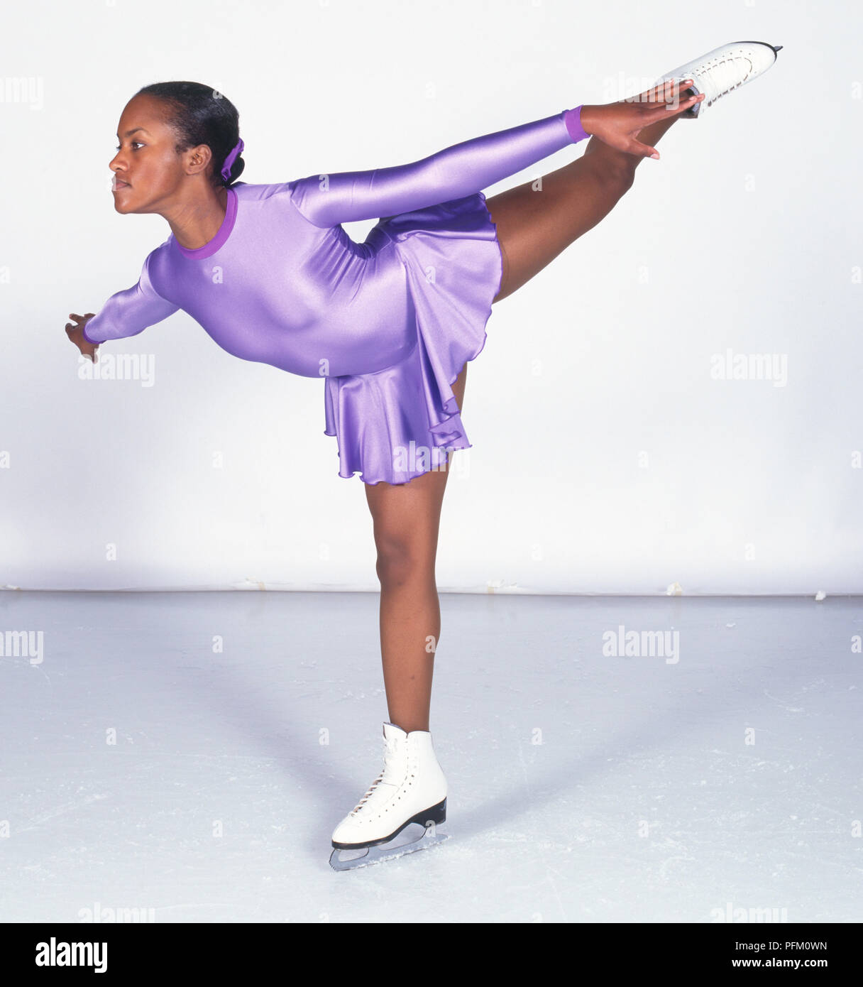 Teenage girl in purple ice skating outfit balancing on one skate, back ...