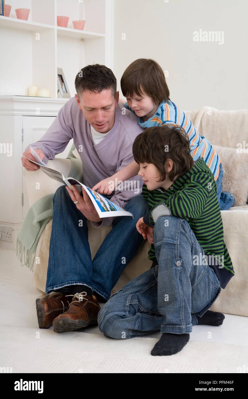 Man and two boys sitting on sofa looking at magazine together Stock ...