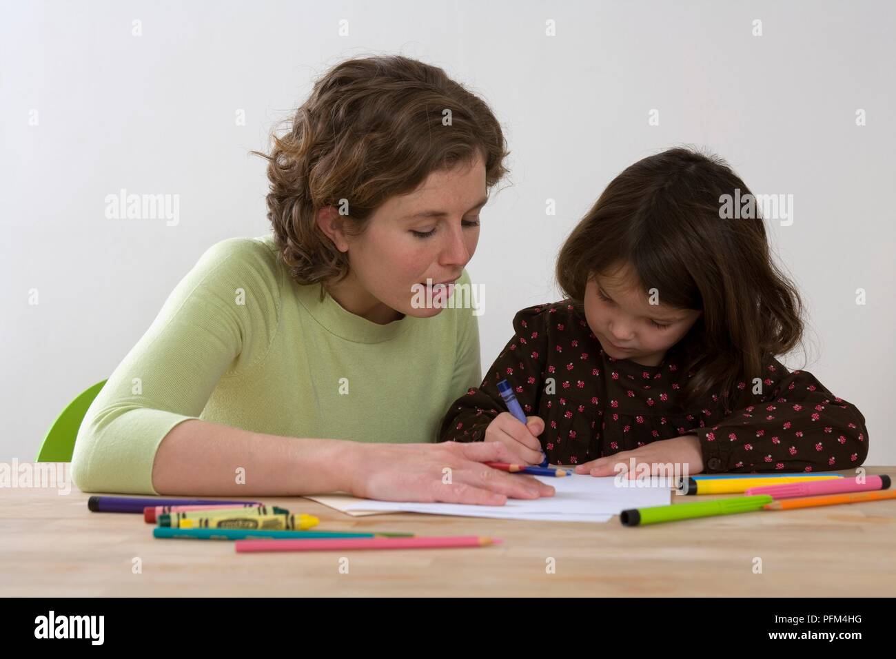 Girl drawing with crayons, woman sitting next to her Stock Photo - Alamy