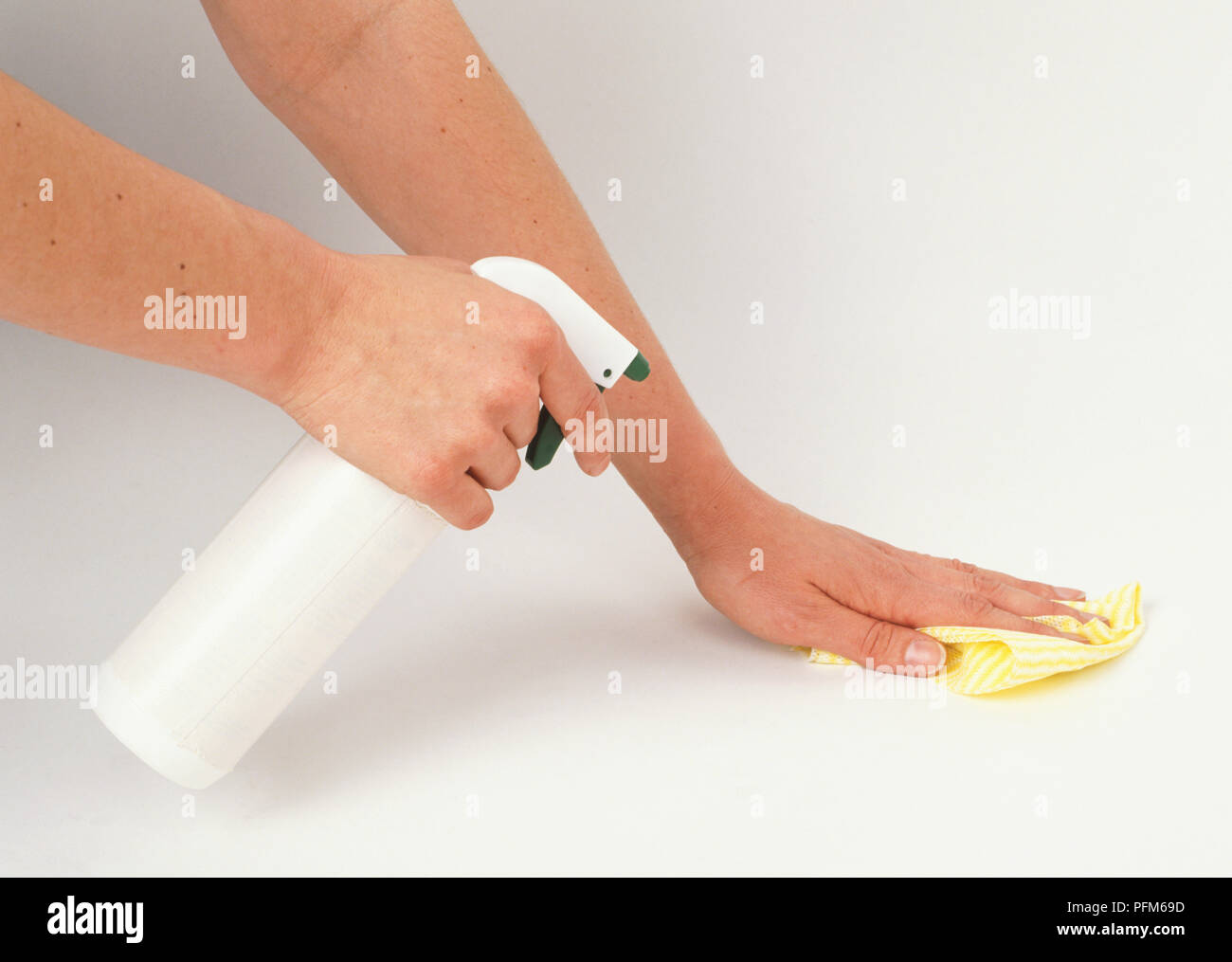 Woman holding spray can in one hand and wiping flat surface with cloth ...