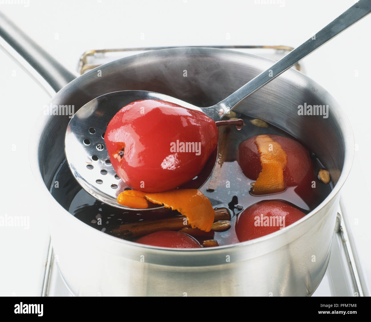 Poached pear on a slotted spoon above a pan of pears Stock Photo - Alamy