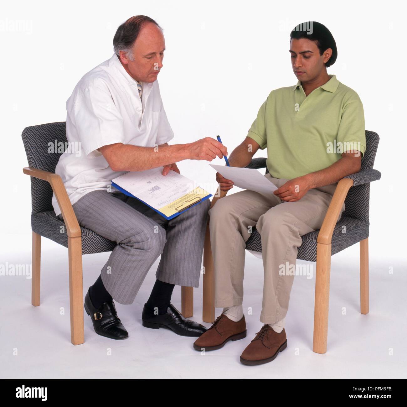 Doctor and patient seated in chairs looking at medical records together ...