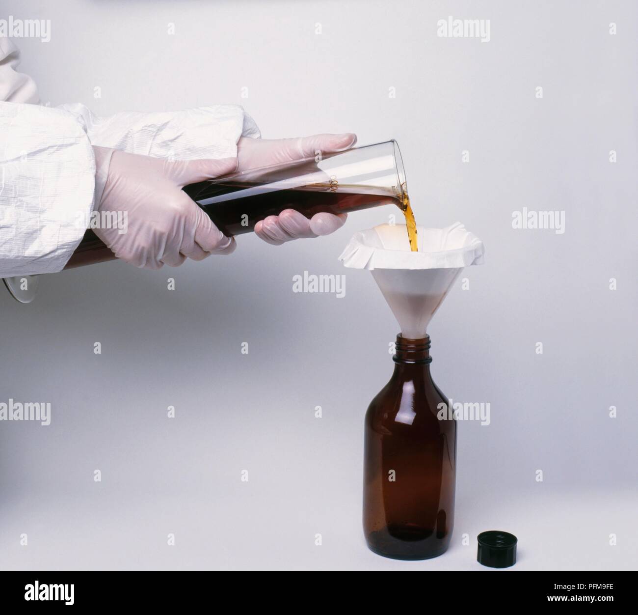 Straining herbal infusion into glass bottle through funnel, close-up ...