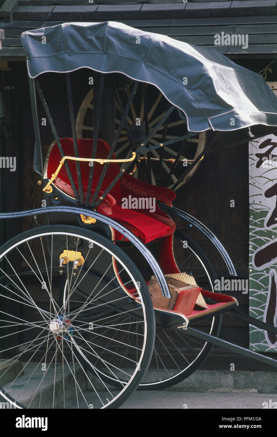 Two-wheeled rickshaw with black canopy, handles resting on floor, side ...
