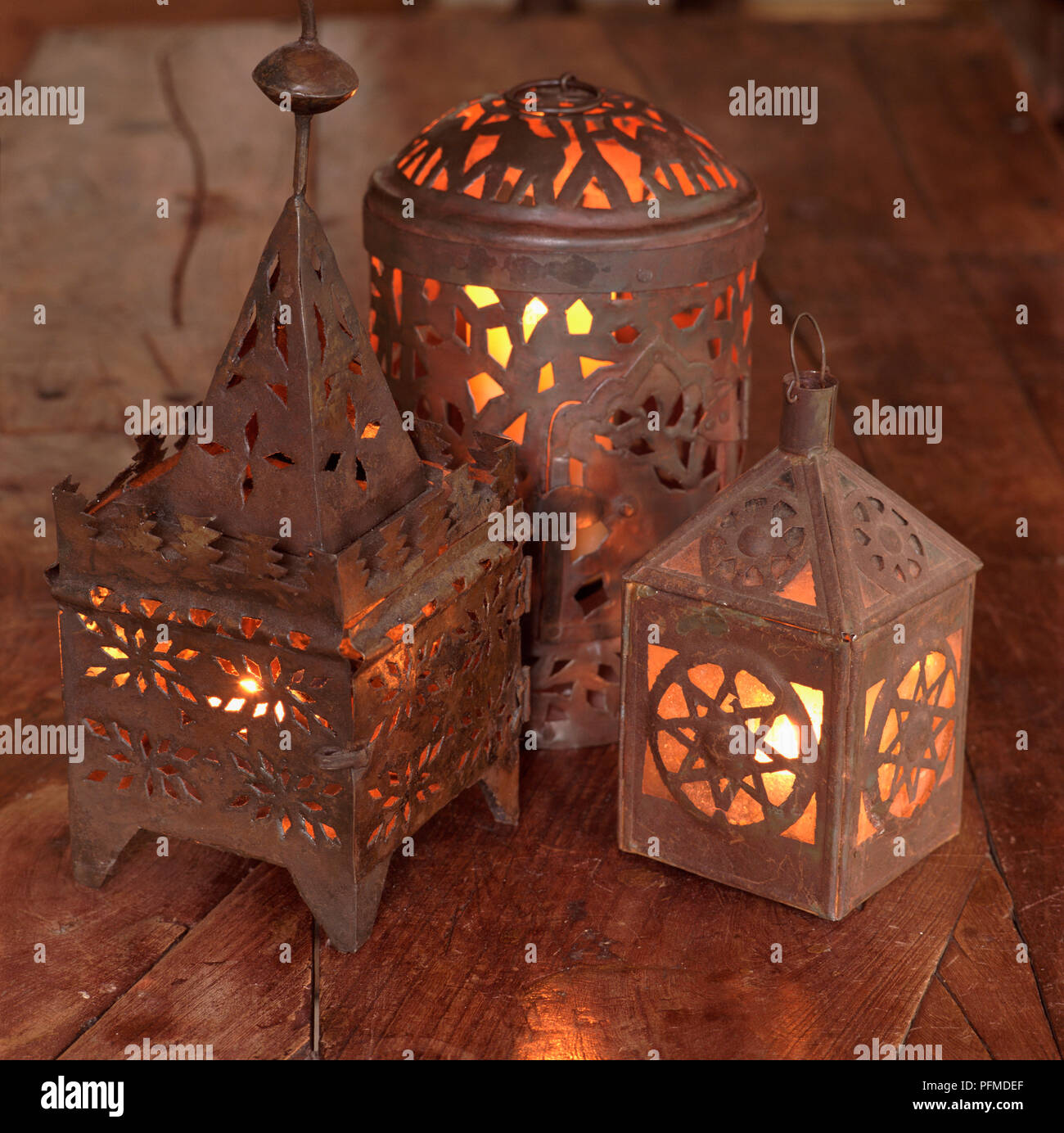 Three iron lanterns with geometric shapes cut out, lit candles glowing ...