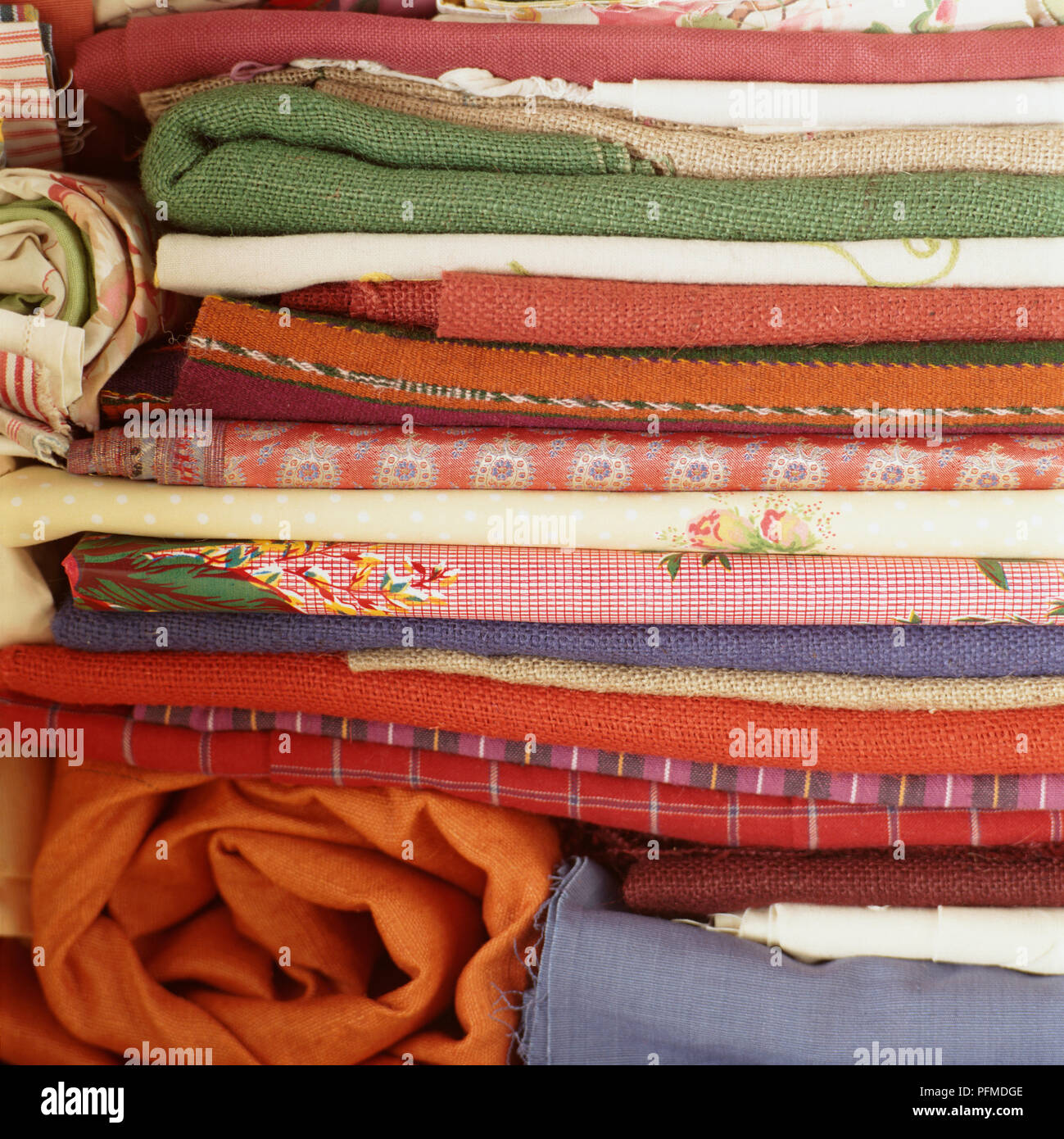 Pile of folded fabrics, assorted colours and patterns, two rolled up ...