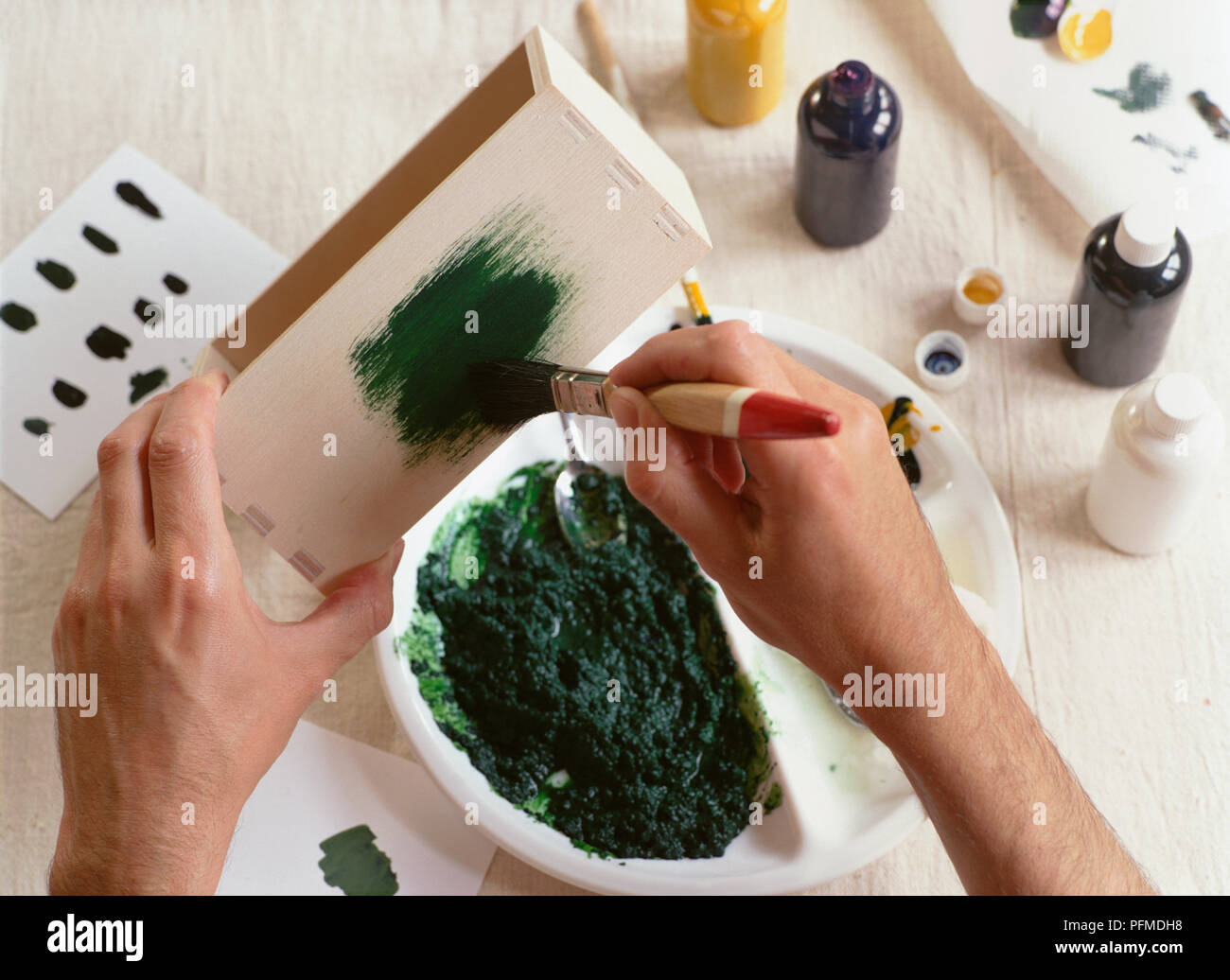 Hands painting dark green paint onto untreated wooden box using ...